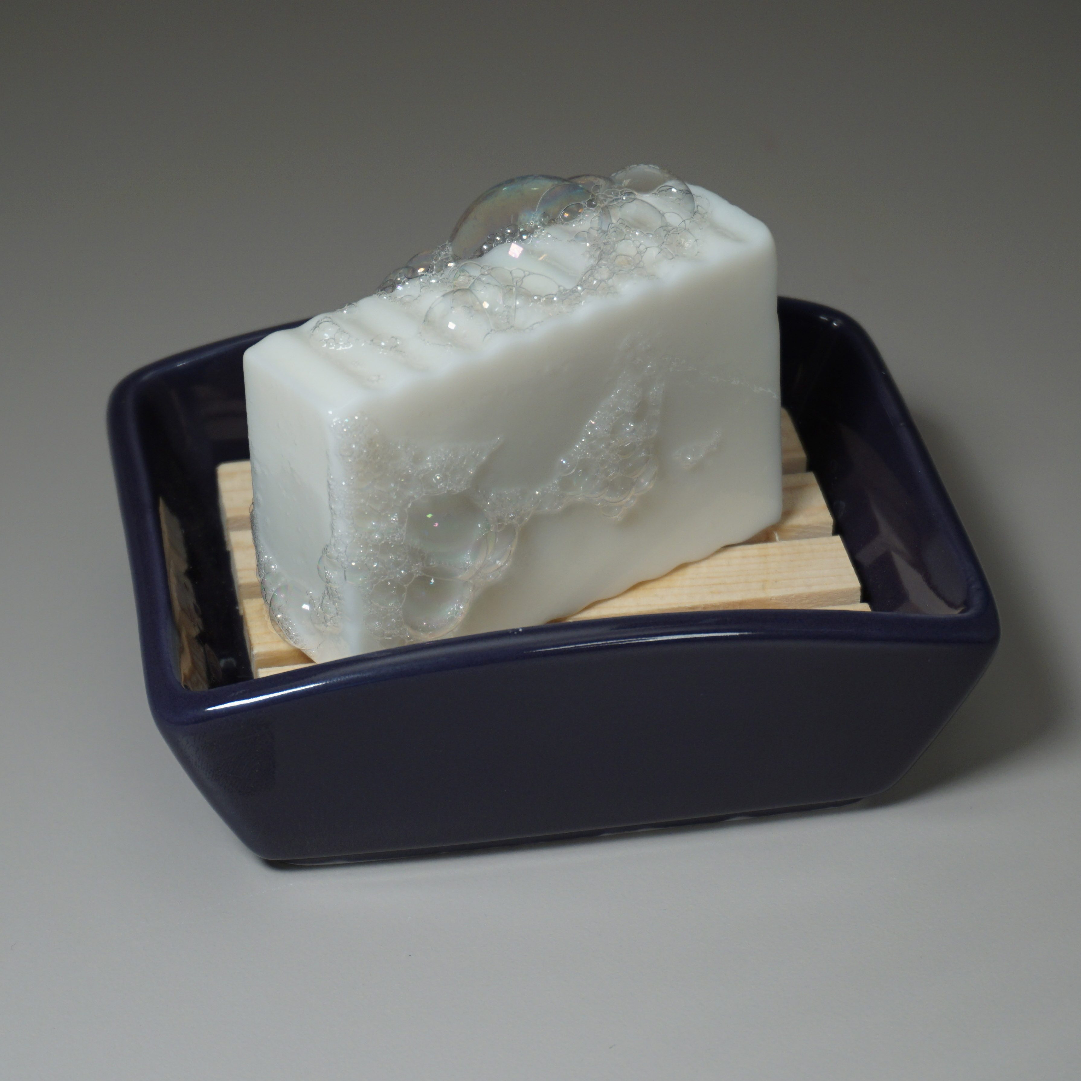 Pure and natural herbal soap displayed wet and bubbly on a dark blue ...